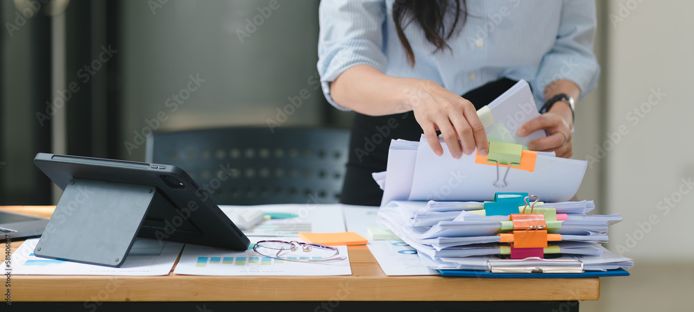 A businesswoman is sifting through stacks of paper files and folders ...