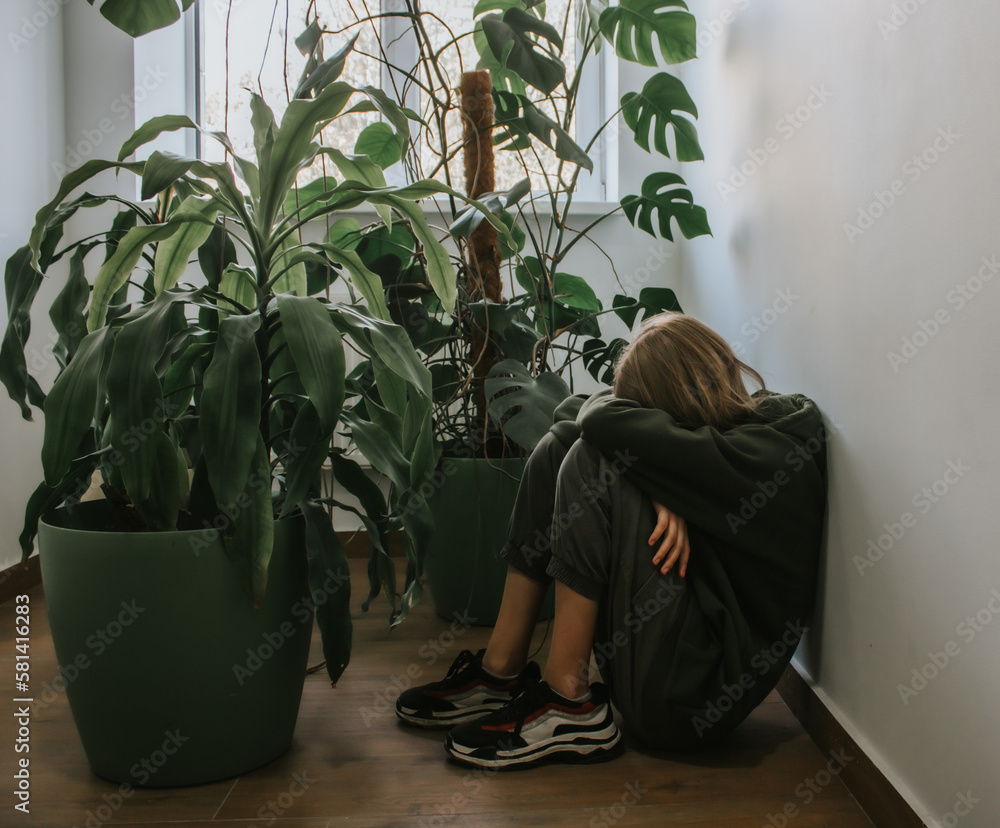 A teenage girl sits with her arms clasped on her knees on the floor ...