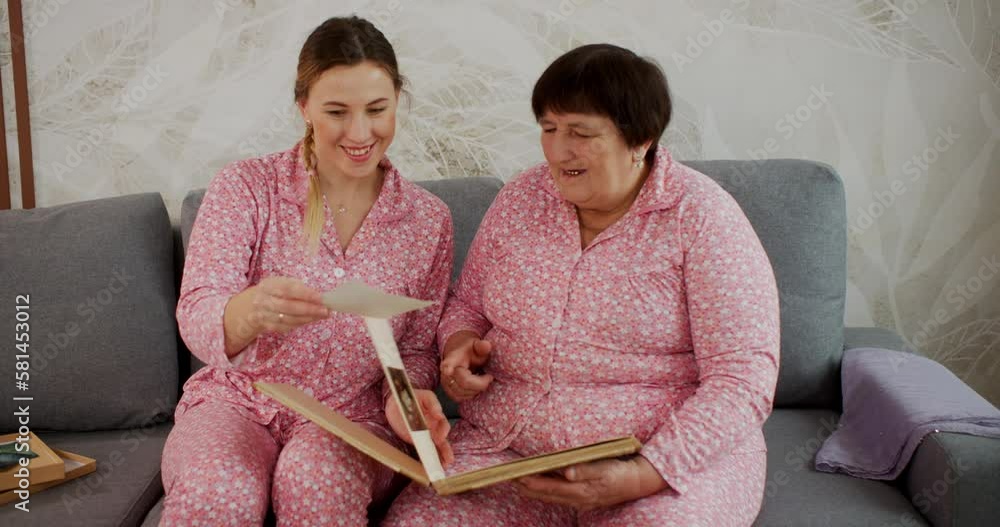 Senior granny and adult granddaughter looking at photos in family album ...