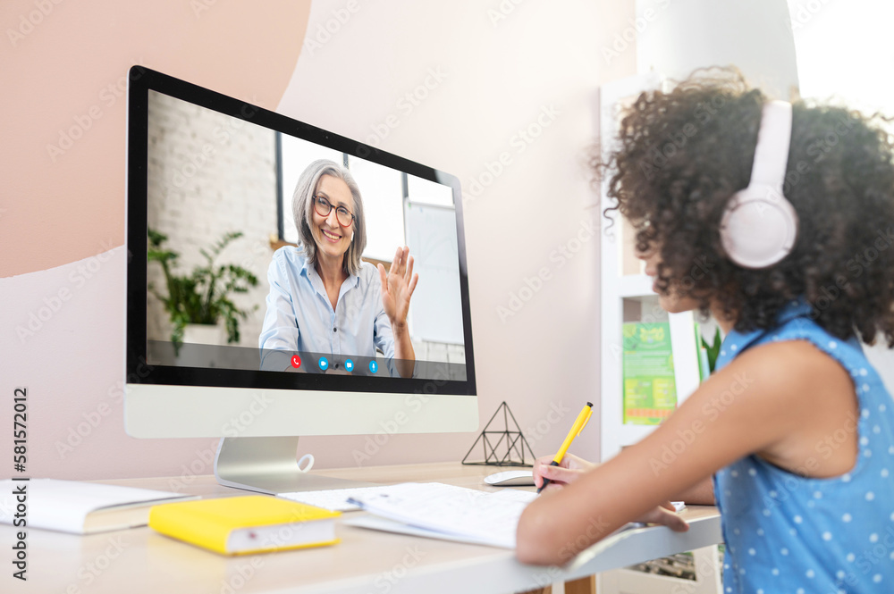 Foto de Senior female teacher on the computer screen greeting her cute ...