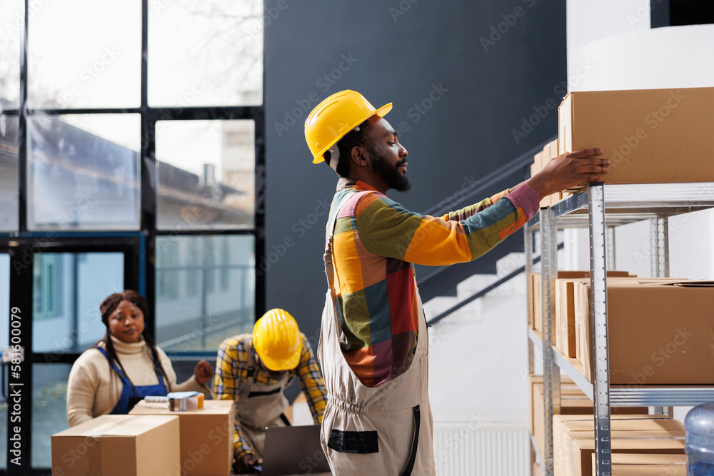 Foto de Warehouse worker in hard hat taking carton from metal shelf ...