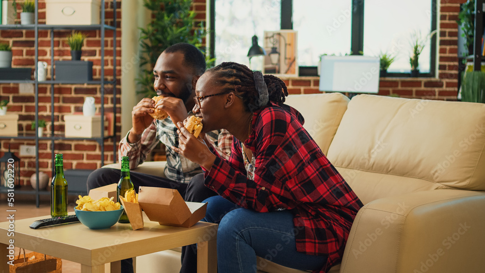 Cheerful young people eating hamburgers and fries in living room ...