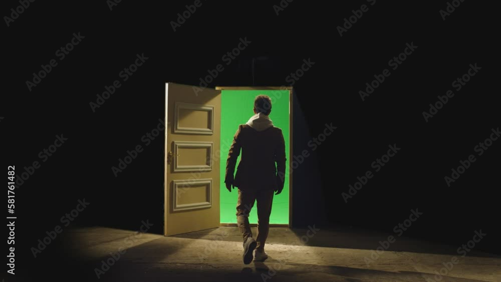 Back view of a man walking in front of an open door with darkness ...