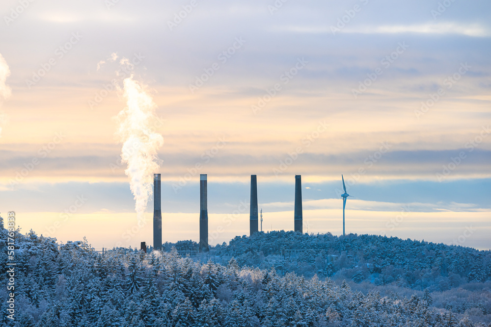 Four smoke stacks and a wind power plant by a forest at winter. Stock ...