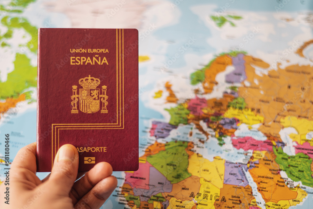 Hand Holding Spanish Passport Against Colorful World Map Atlas. Concept ...