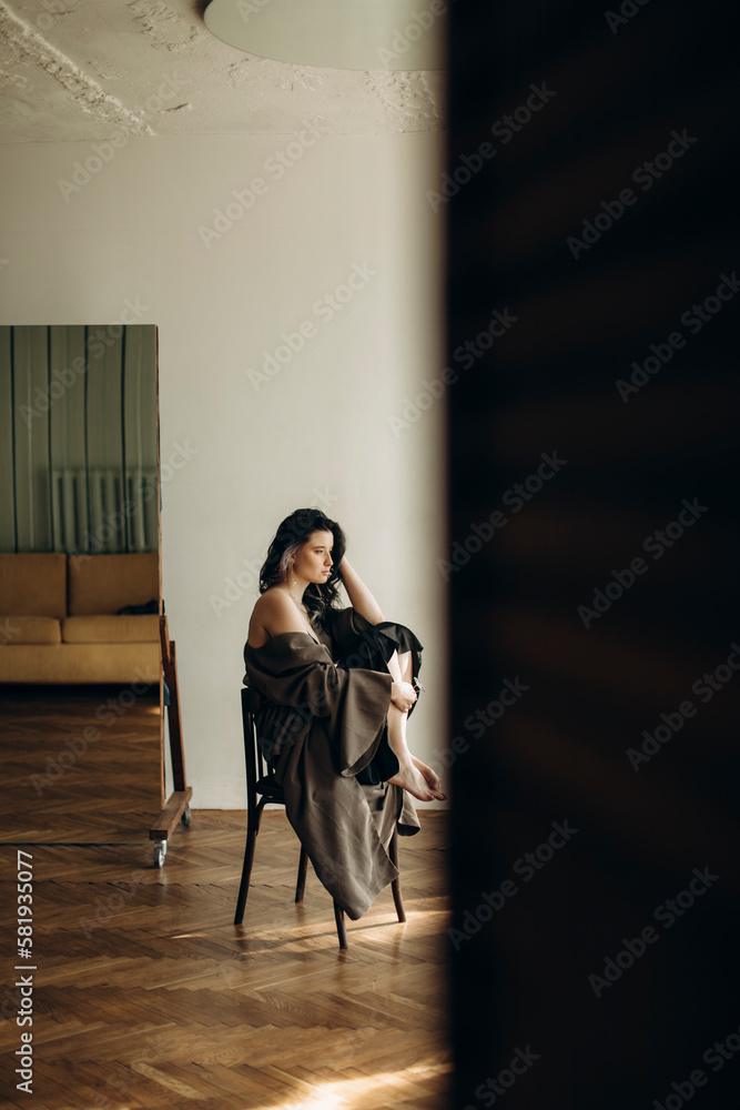 young beautiful brunette woman sits sideways on a chair in a room with ...