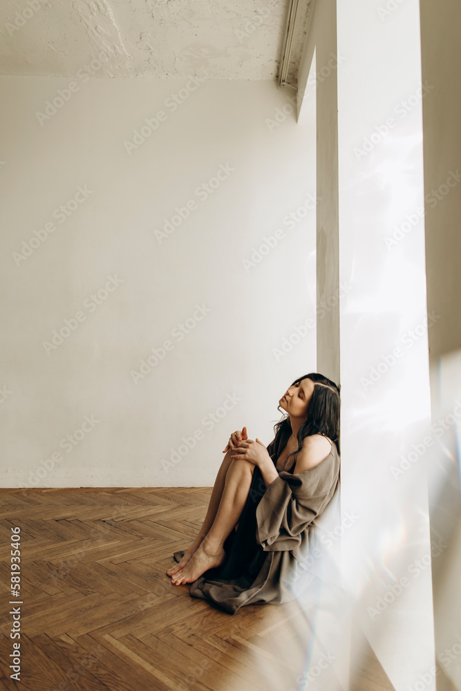 young beautiful woman sits on the floor with her back against the wall ...