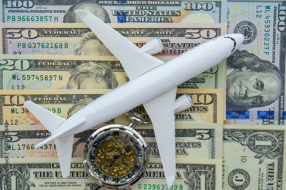 Passenger plane and pocket watch sitting on US currency bills of ...