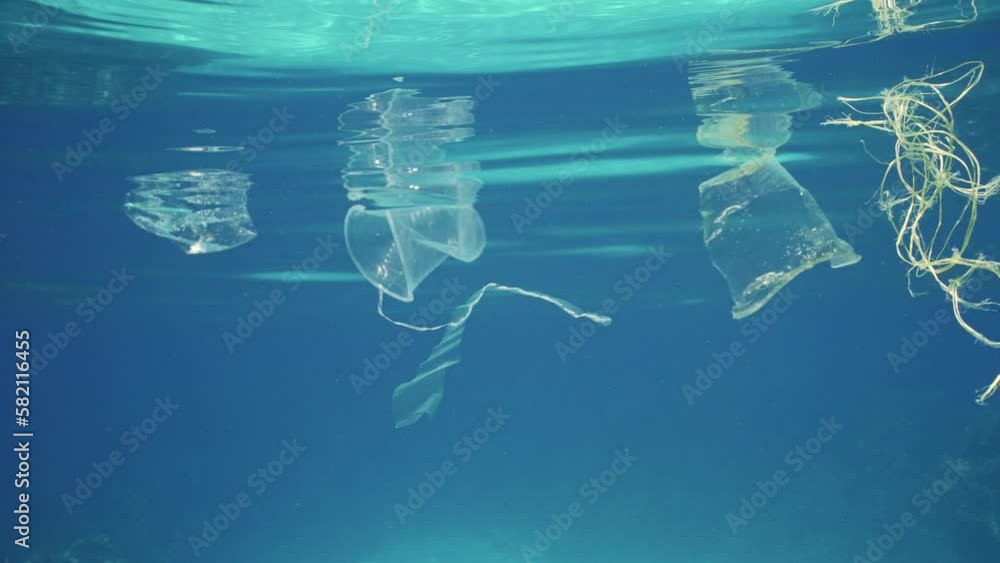 Plastic debris floating below surface in blue water, Slow motion ...