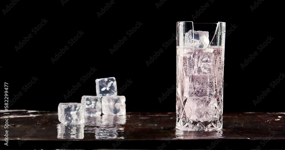 Icecube splashing to glass of cold sparkling drink and breaking glass ...