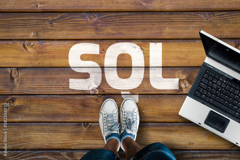 Legs in sneakers standing next to laptop and SQL on wooden floor. SQL ...