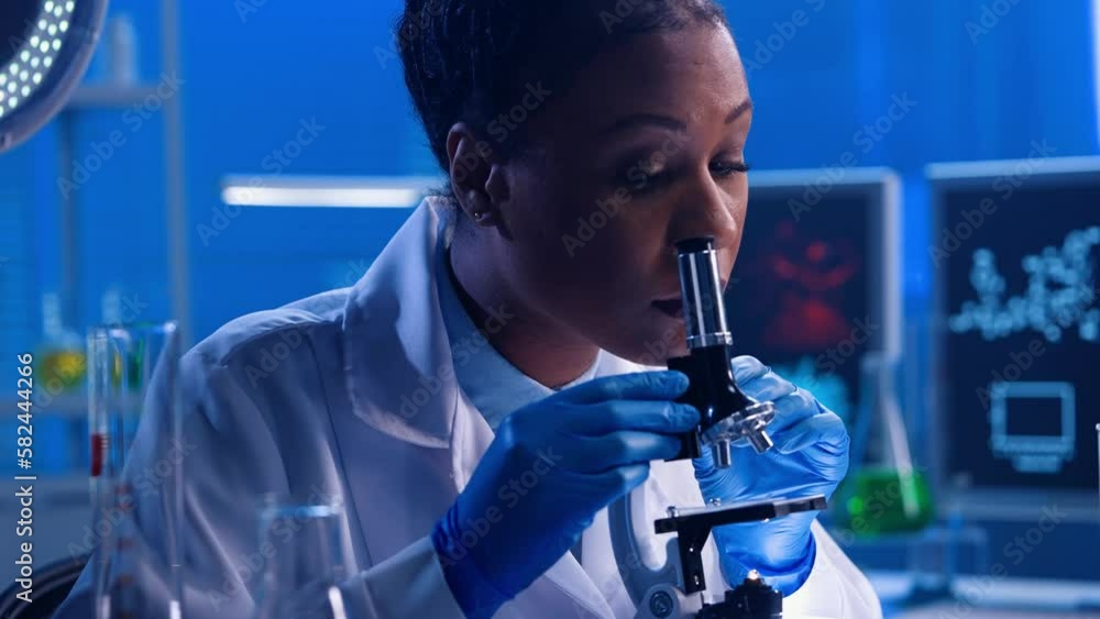A young African American woman examines a specimen under a microscope ...