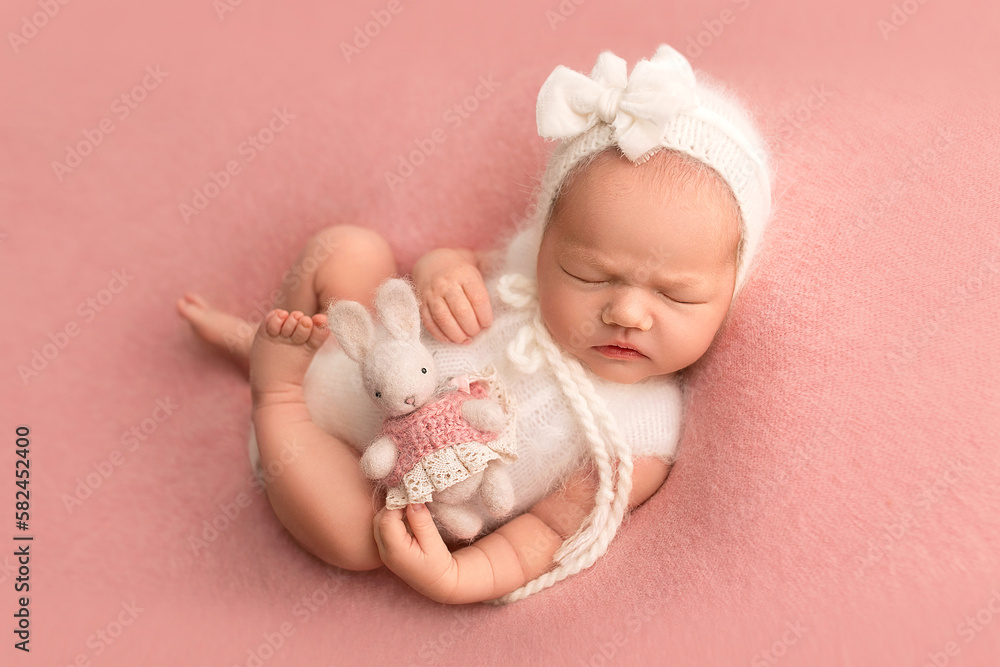 Top view of a newborn baby girl sleeping in a white overalls, with a white cap on her head. With ...