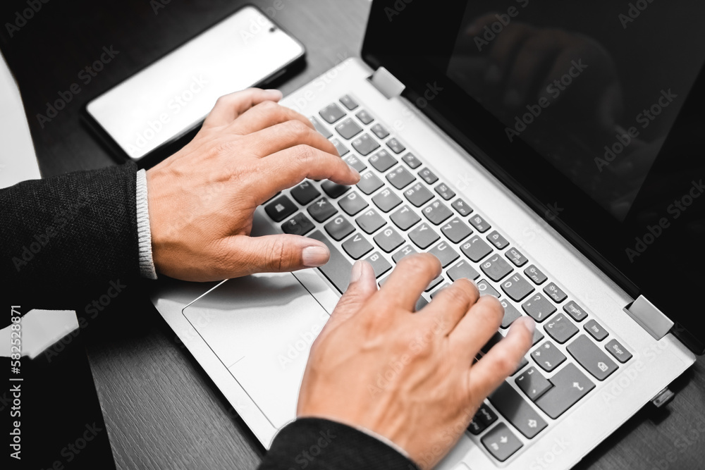 Man working on his desktop computer, next to a cell phone with a white ...