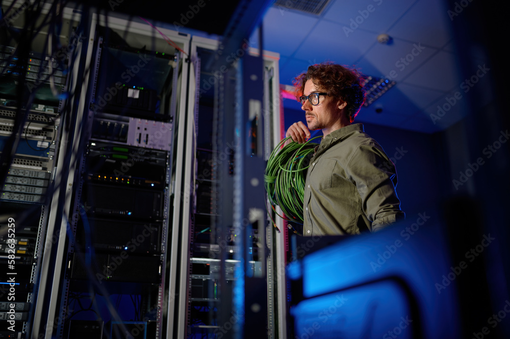 Data center engineer with many optic wires cables walking next to ...