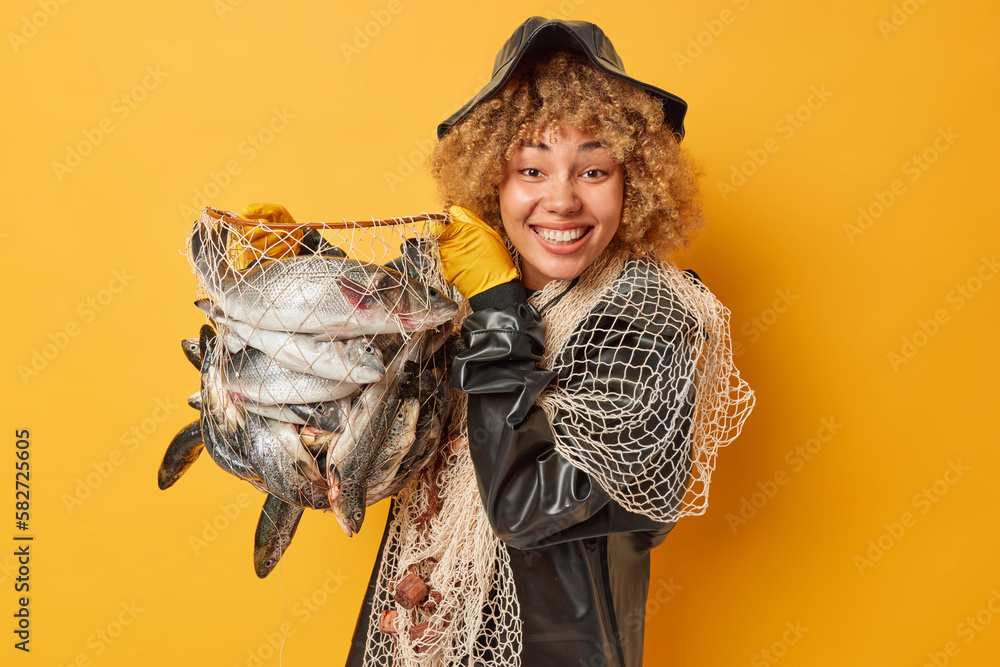 Horizontal shot of cheerful curly haired female angler holds fishing ...