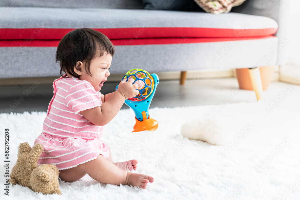 7-month-old baby girl sitting on the floor playing a toys, which is the ...