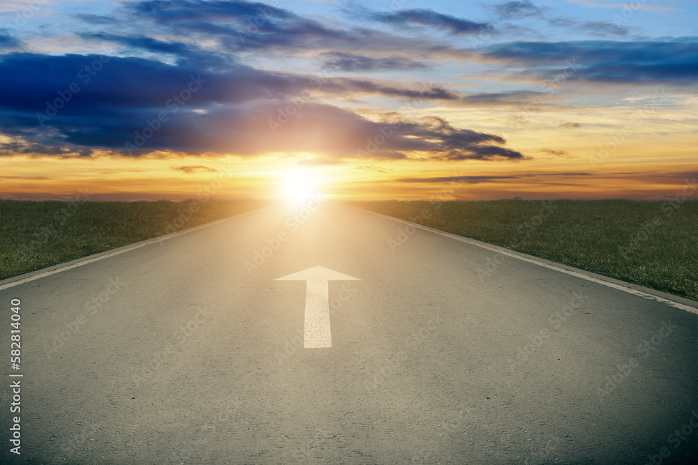 Asphalt road with white arrow sign goes to horizon. Sunshine on horizon ...