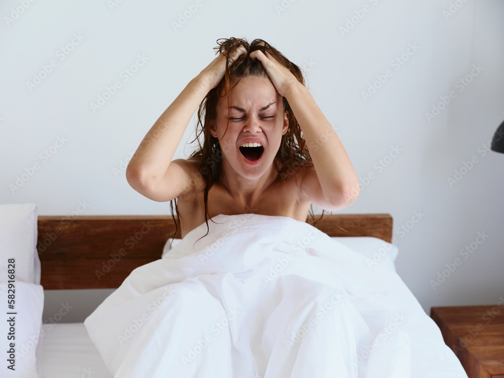An angry woman sits on a bed in the bedroom and covers her body with a ...