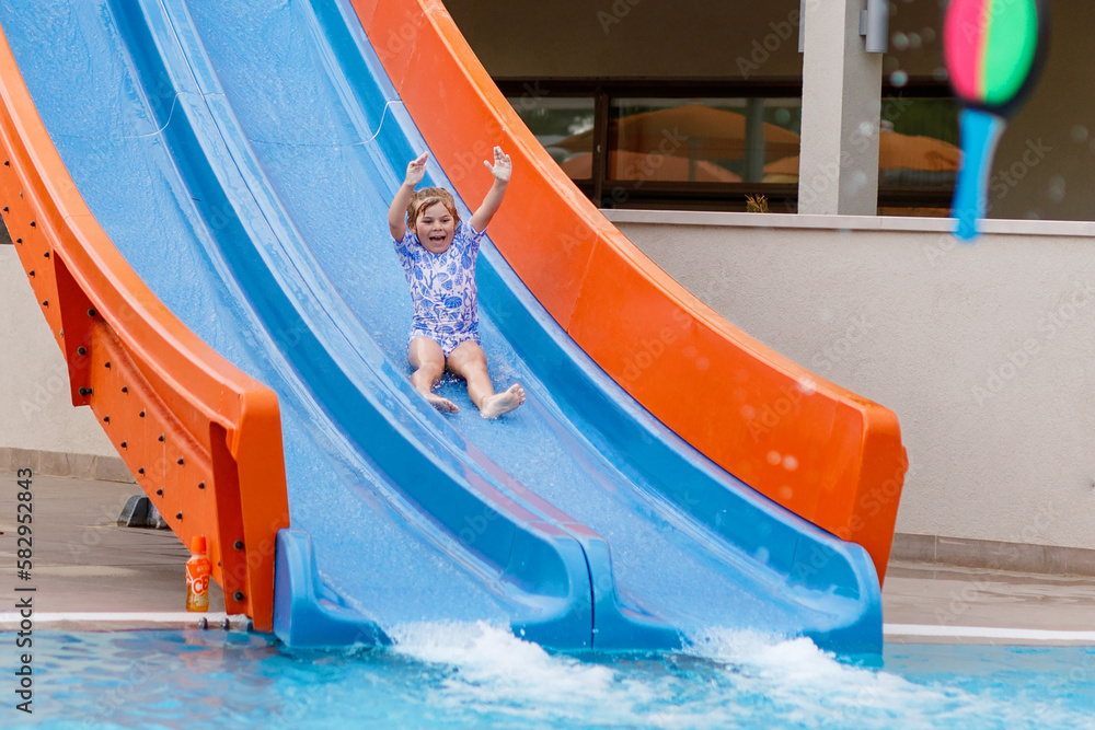 Little preschool girl sliding on a children slide in outdoor swimming ...