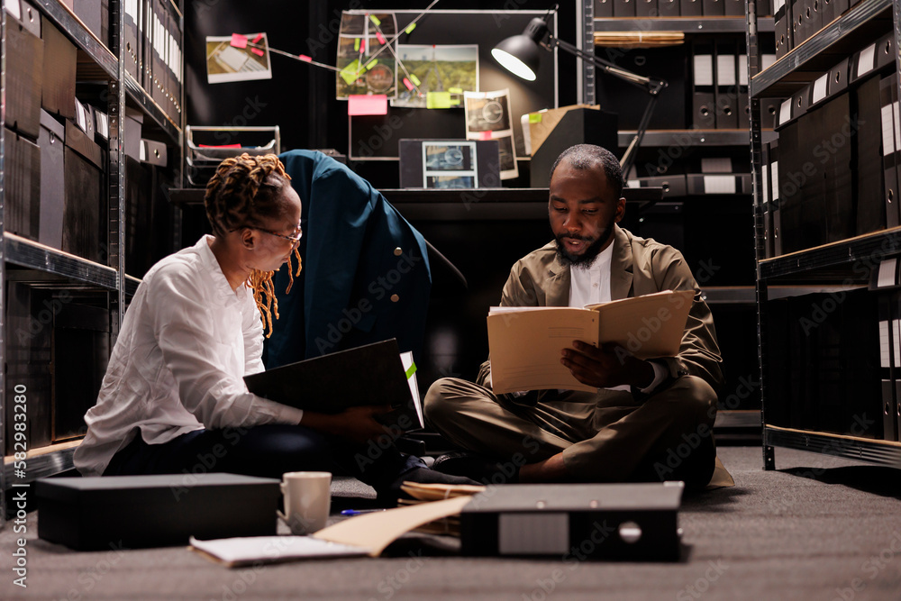 Police detective partners sitting on floor surrounded by case files ...