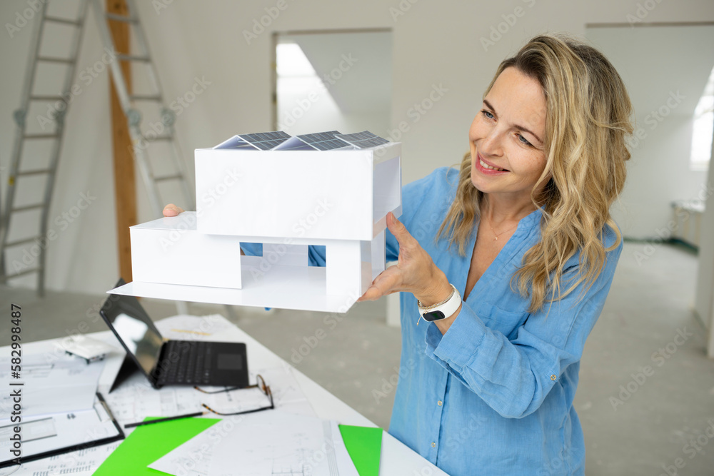 Smiling architect holding and examining model home at construction site ...