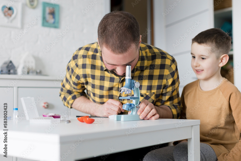 Smiling boy sitting by father looking through microscope at table Stock ...