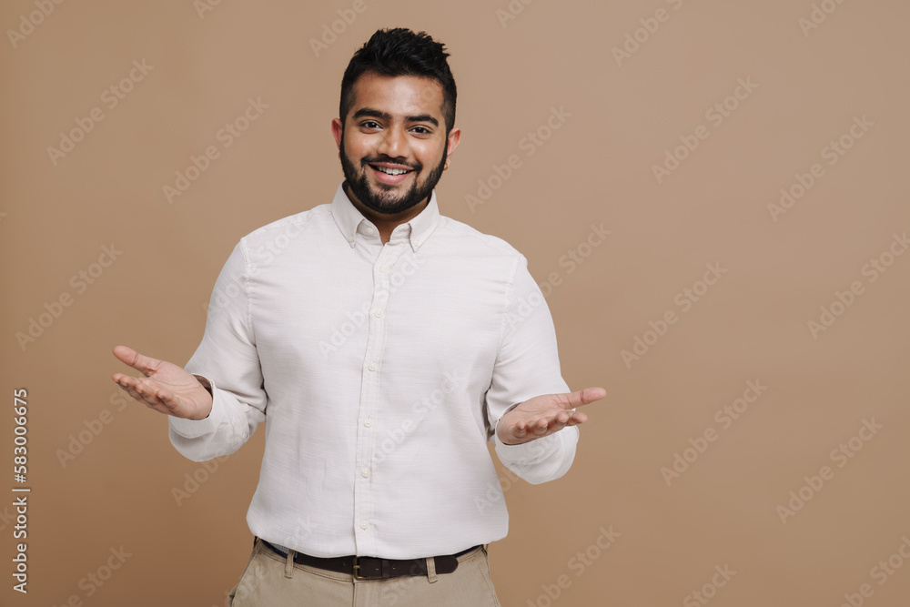 Positive indian man shrugging shoulders isolated over beige background ...
