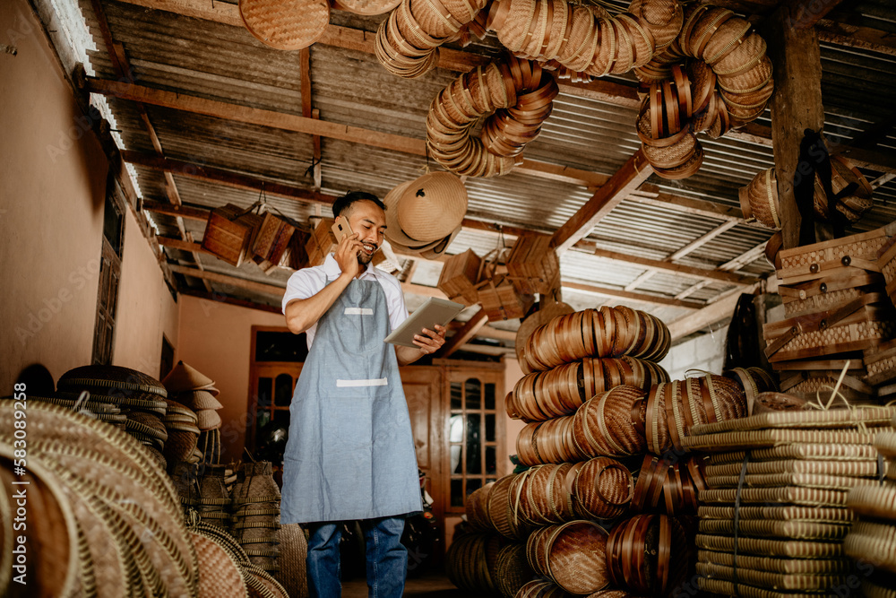 young asian male craft business owner having a phone call while working ...