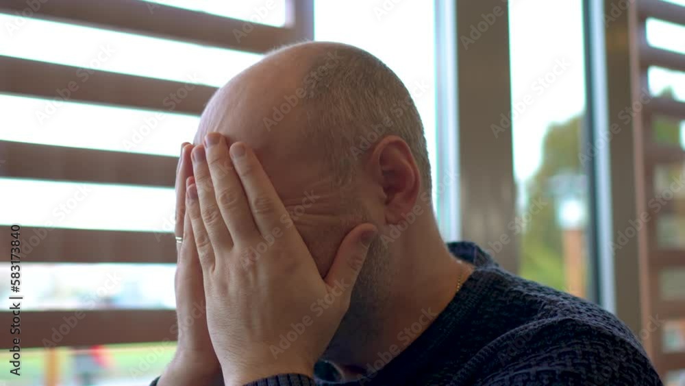 Depressed tired man sitting on bar counter and rubs his face with hands ...