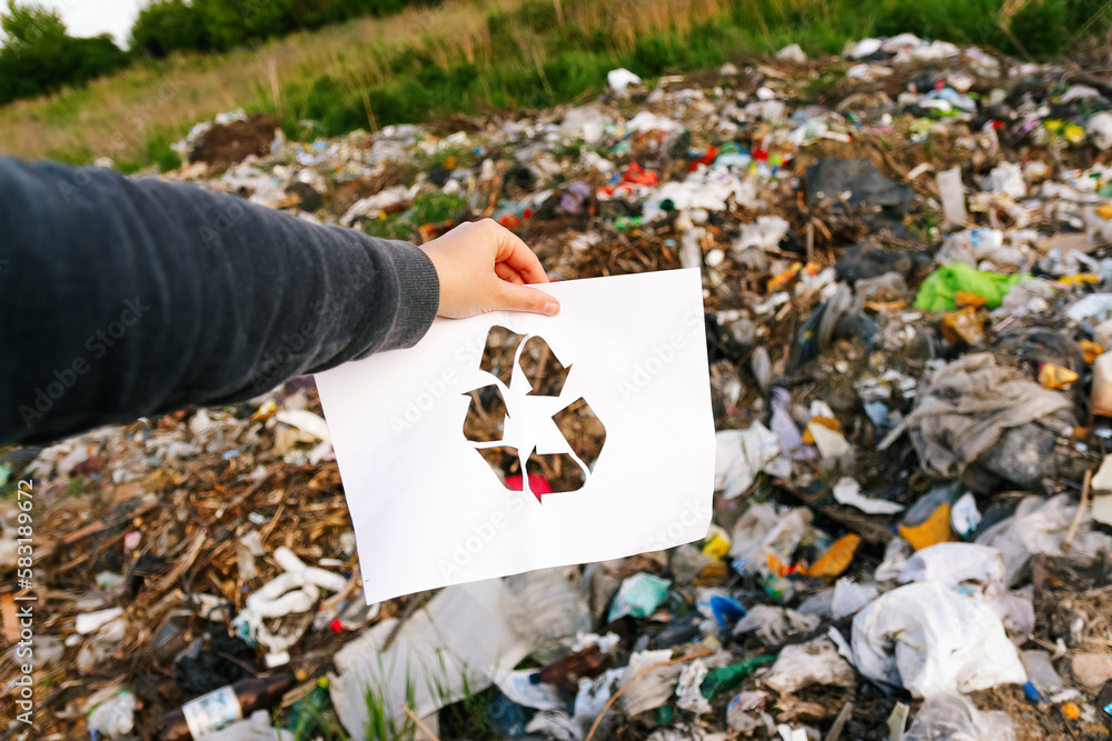 Garbage pollution. Hand holding cut paper with the logo of recycling on ...
