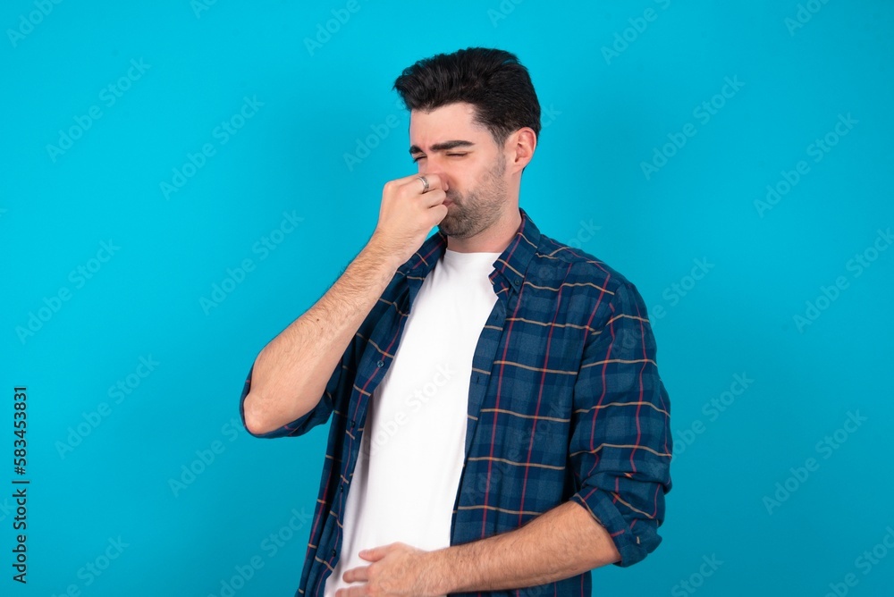 Young man standing over blue studio background smelling something ...