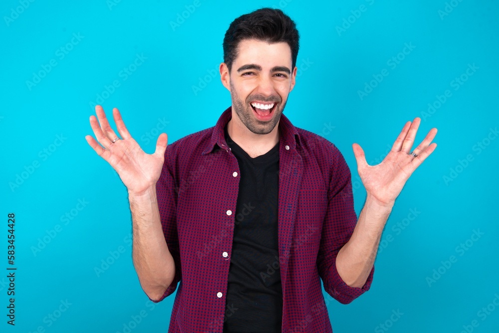 Crazy outraged Young man standing over blue studio background screams ...