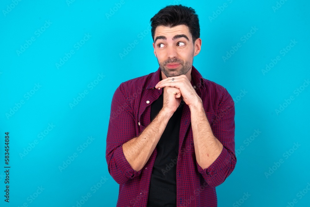 Curious Young man standing over blue studio background keeps hands ...