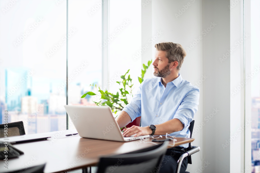 Confident professional man sitting at office desk and usin laptop for ...