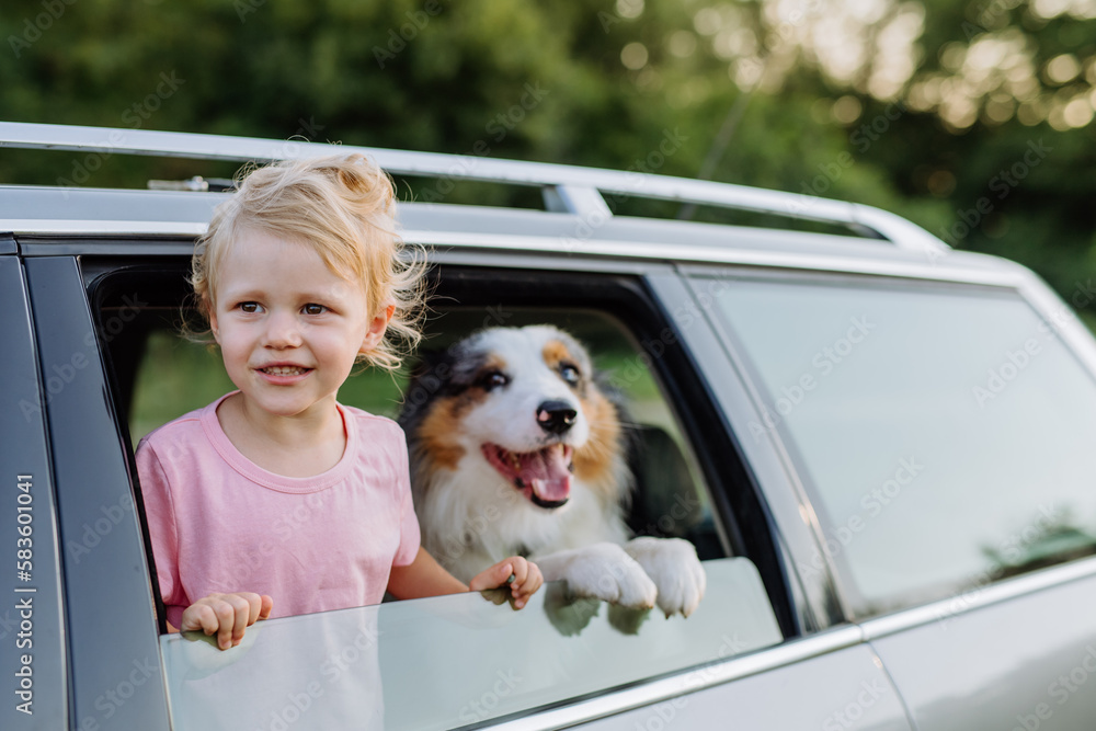 Little girl and her dog sitting in a car, prepared for family trip ...