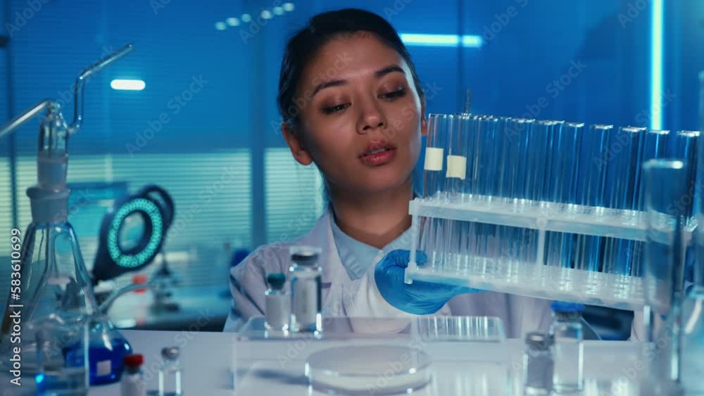 An Asian woman doctor puts a stand with test tubes on the shelf of a ...