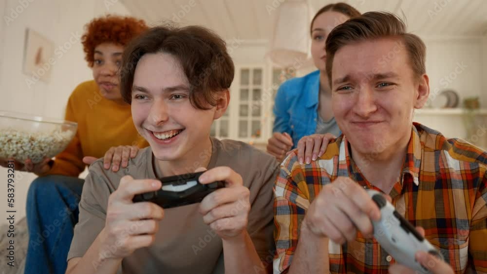 Two guys competing playing video games and girls cheering them. One guy ...