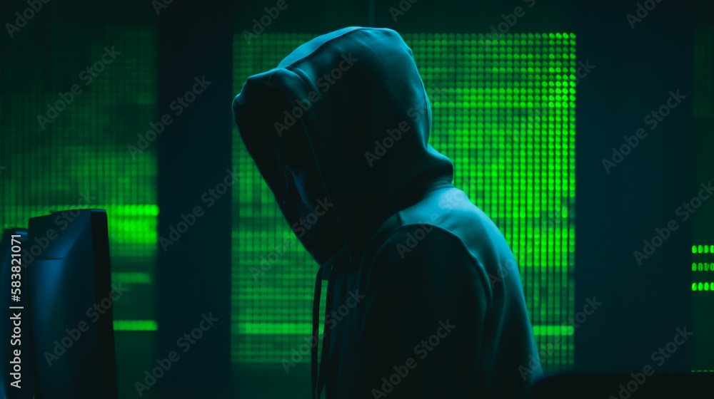 Hacker with hoodie in front of the monitor with green background ...