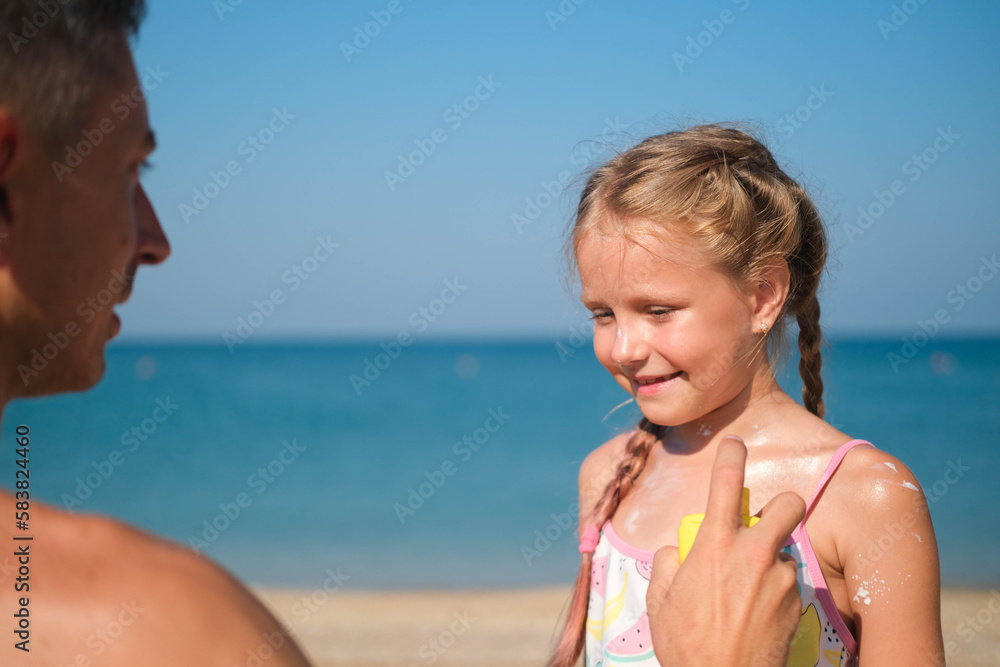 Father applying protective cream to her daughter's face at the beach. Man hand holding sunscreen ...