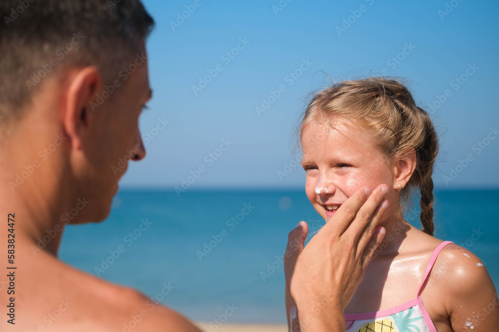 Father applying protective cream to her daughter's face at the beach. Man hand holding sunscreen ...