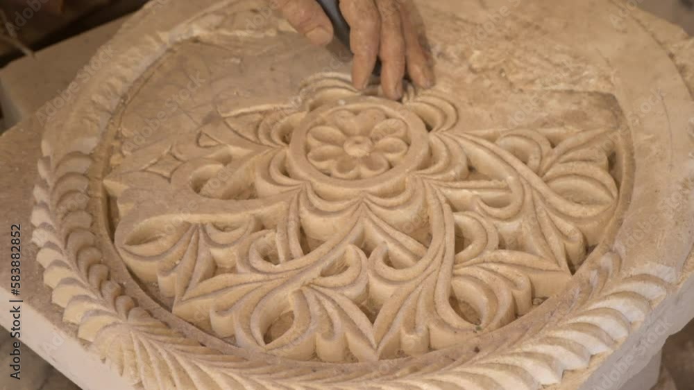 we see a stone ornament artist working on a white stone with a hammer ...