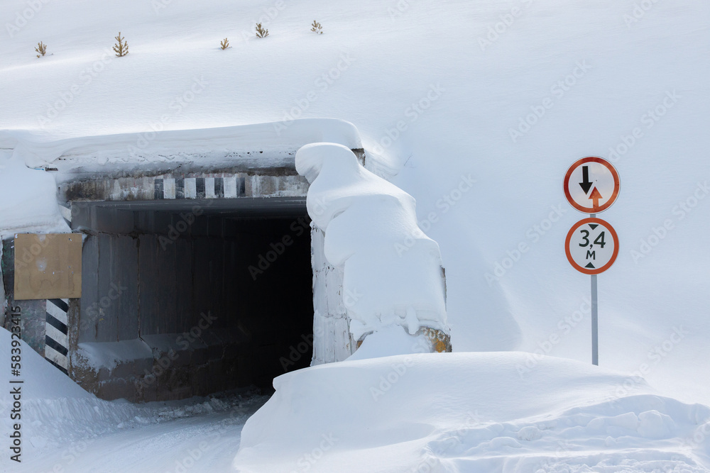 Snowbound narrow country road going through rectangular concrete tunnel ...