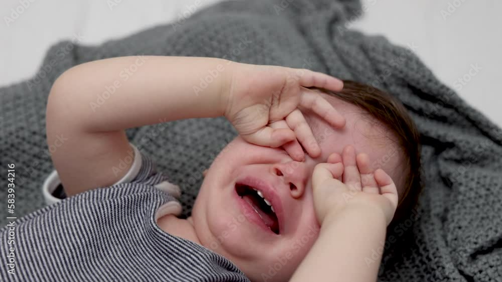 crying baby lying on bed rubbing eyes with hands.angry sleepy upset ...