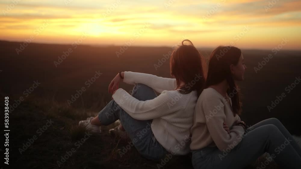 Two teenage girls sit on top of a rock and enjoy the summer sunset ...