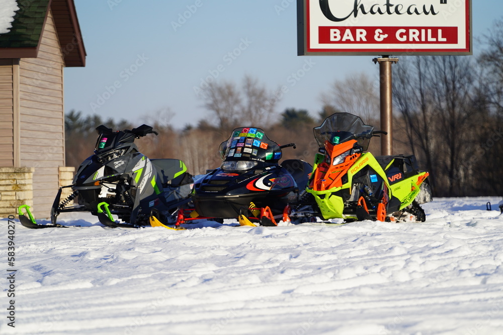 Various types of snowmobiles sit parked out in the Winter snow season ...
