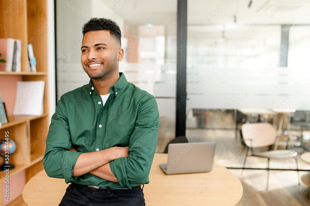 Thriving Indian male employee stands confidently with his arms folded ...