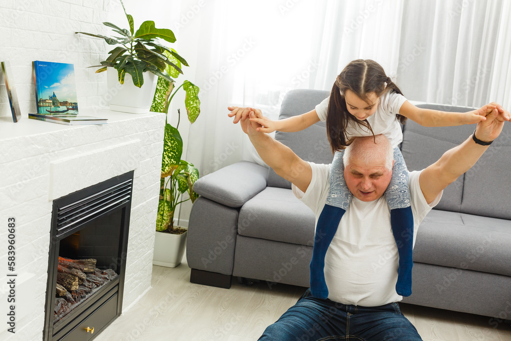 Cute little girl spending time with positive active grandpa in living ...