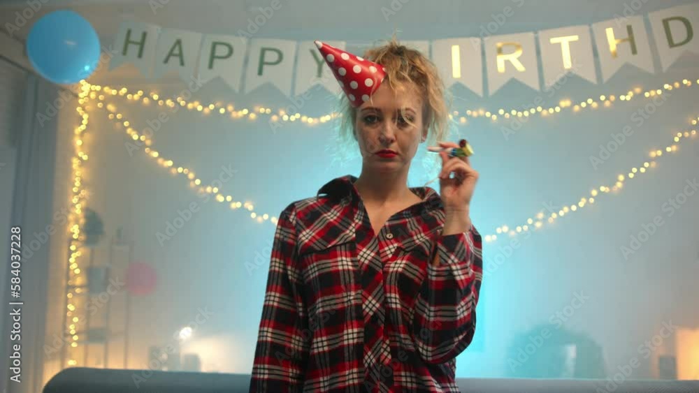 A sad woman with a party cap blowing a party wistle with sadness in her ...