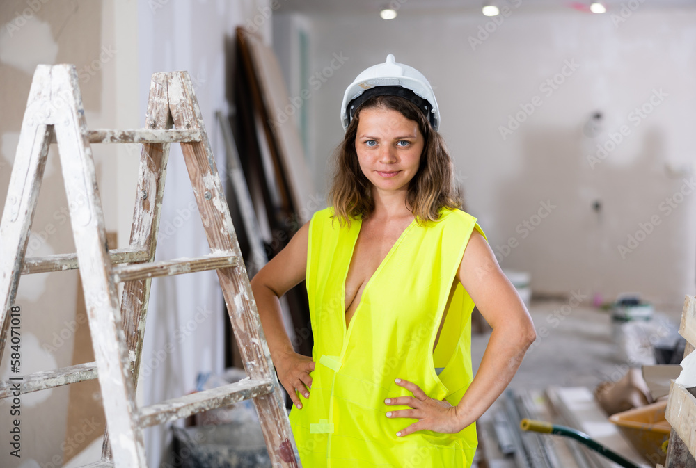 Sexy young woman in a yellow vest and protective helmet poses playfully ...